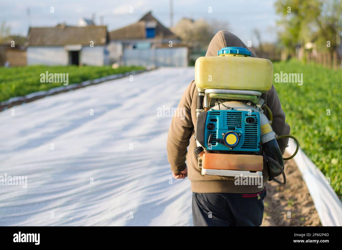 A farmer with a mist sprayer on his back walks through the farm field ...