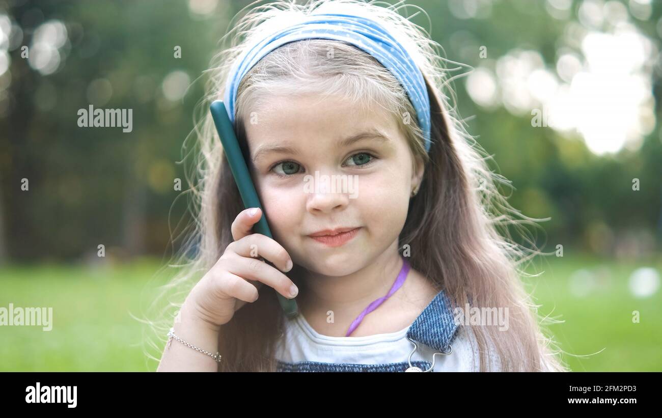 Happy little child girl having conversation talking on her sellphone in ...