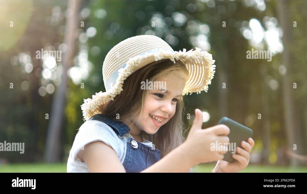 Happy smiling child girl watching in her mobile phone outdoors in ...