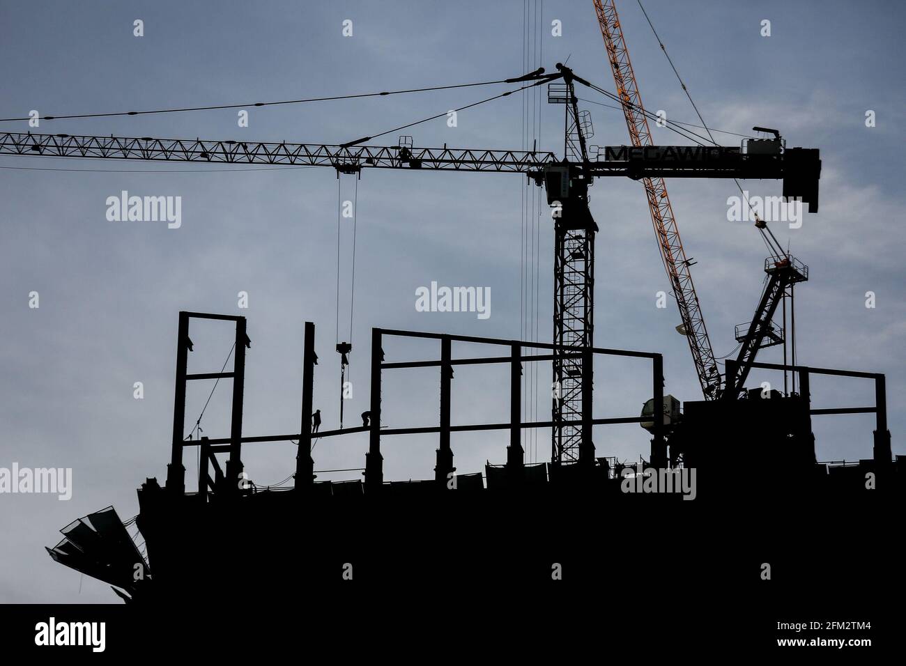 Workers stand on metal beams at a building construction site in ...
