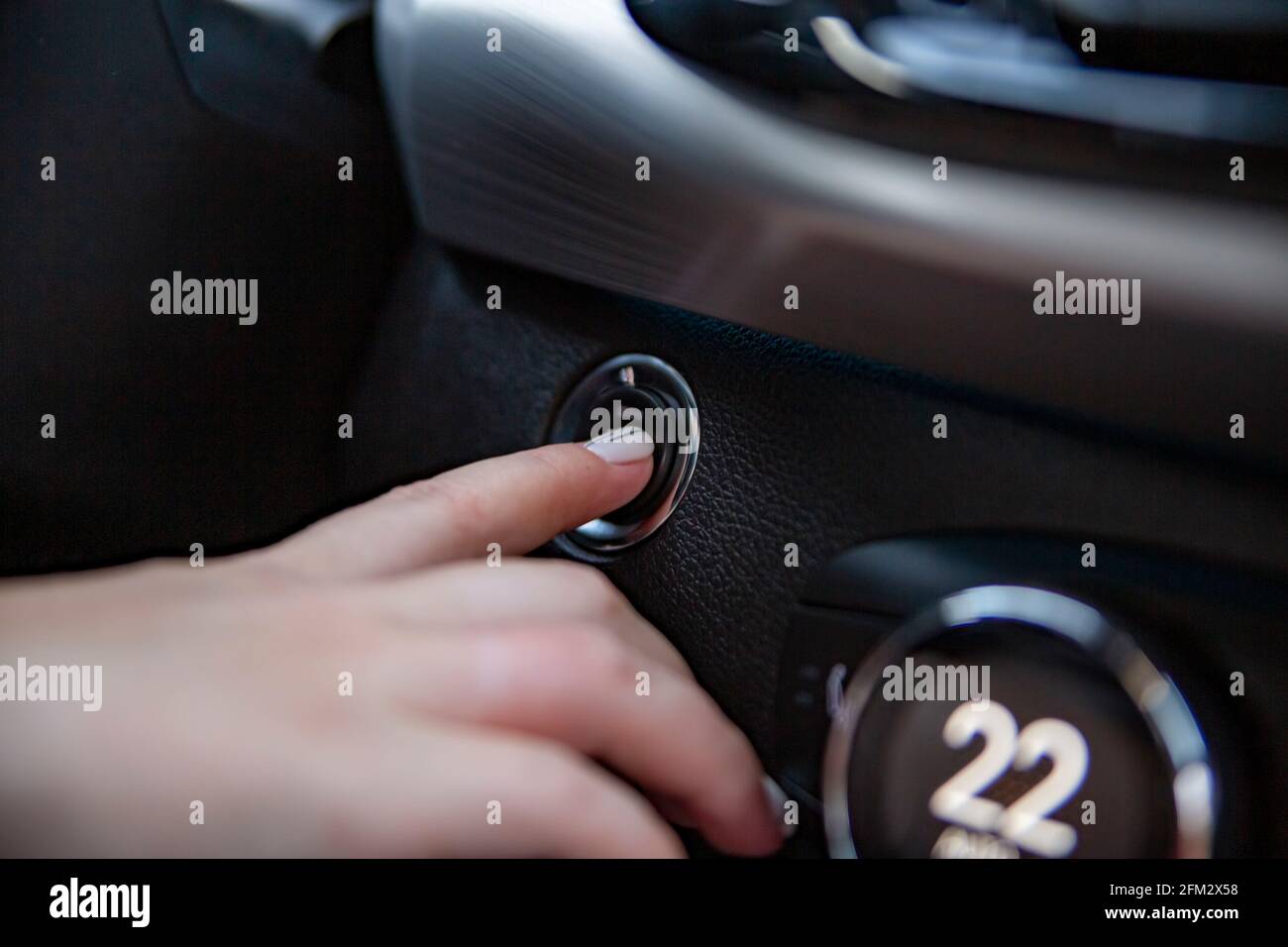 drivers hand finger presses the start stop button in a modern car ...