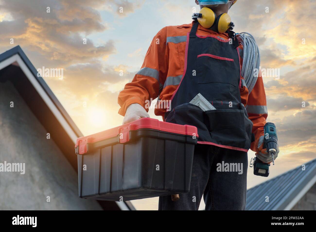 Portrait of an electrician wearing a face mask carrying a toolbox ...