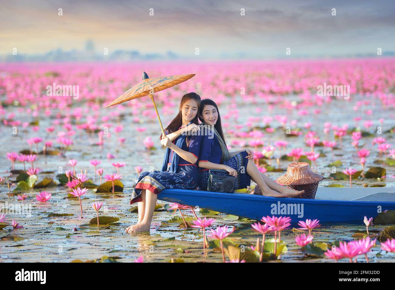 Two beautiful women sailing on a lake with pink lotus flowers, Thailand ...