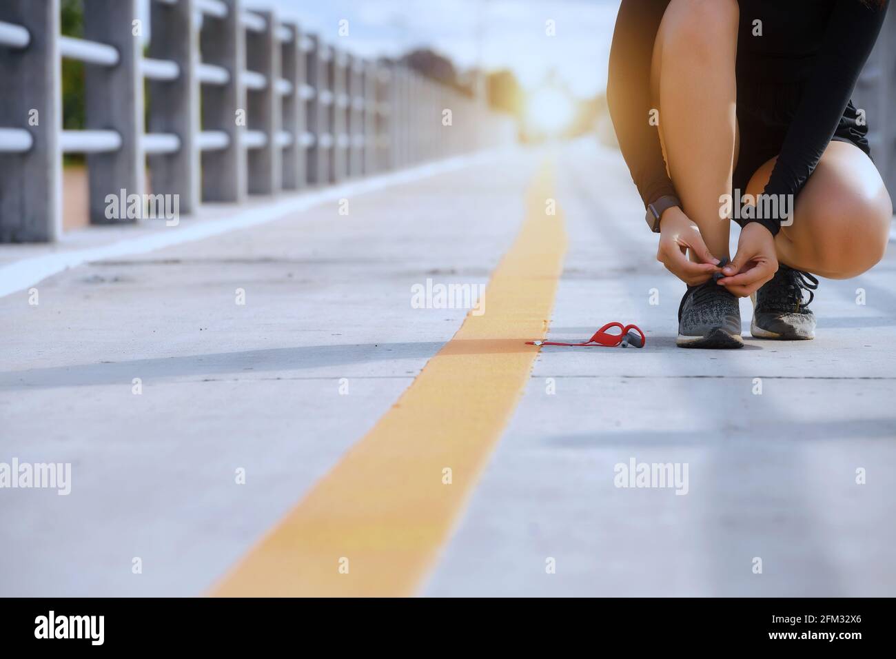 Female runner crouching on a bridge tying her shoelaces, Thailand Stock ...