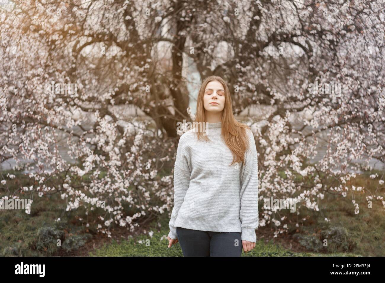Teenage girl with closed eyes next to the tree in flowers spring time ...