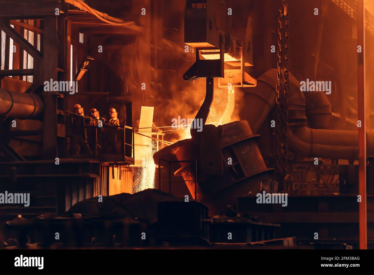 Molten iron pouring from ladle container into mold, workers control ...