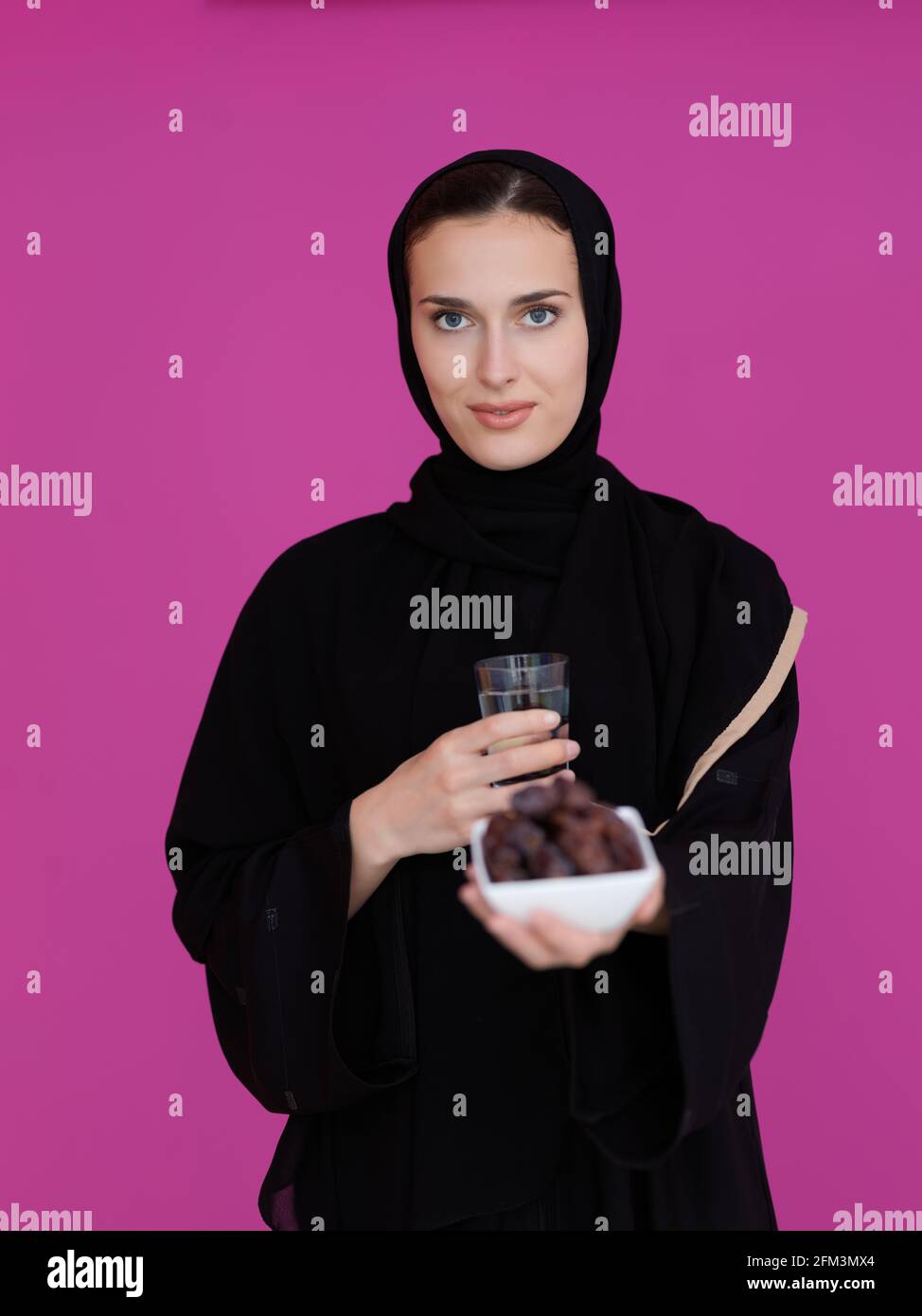 Modern muslim woman in abaya holding a date fruit and glass of water in ...