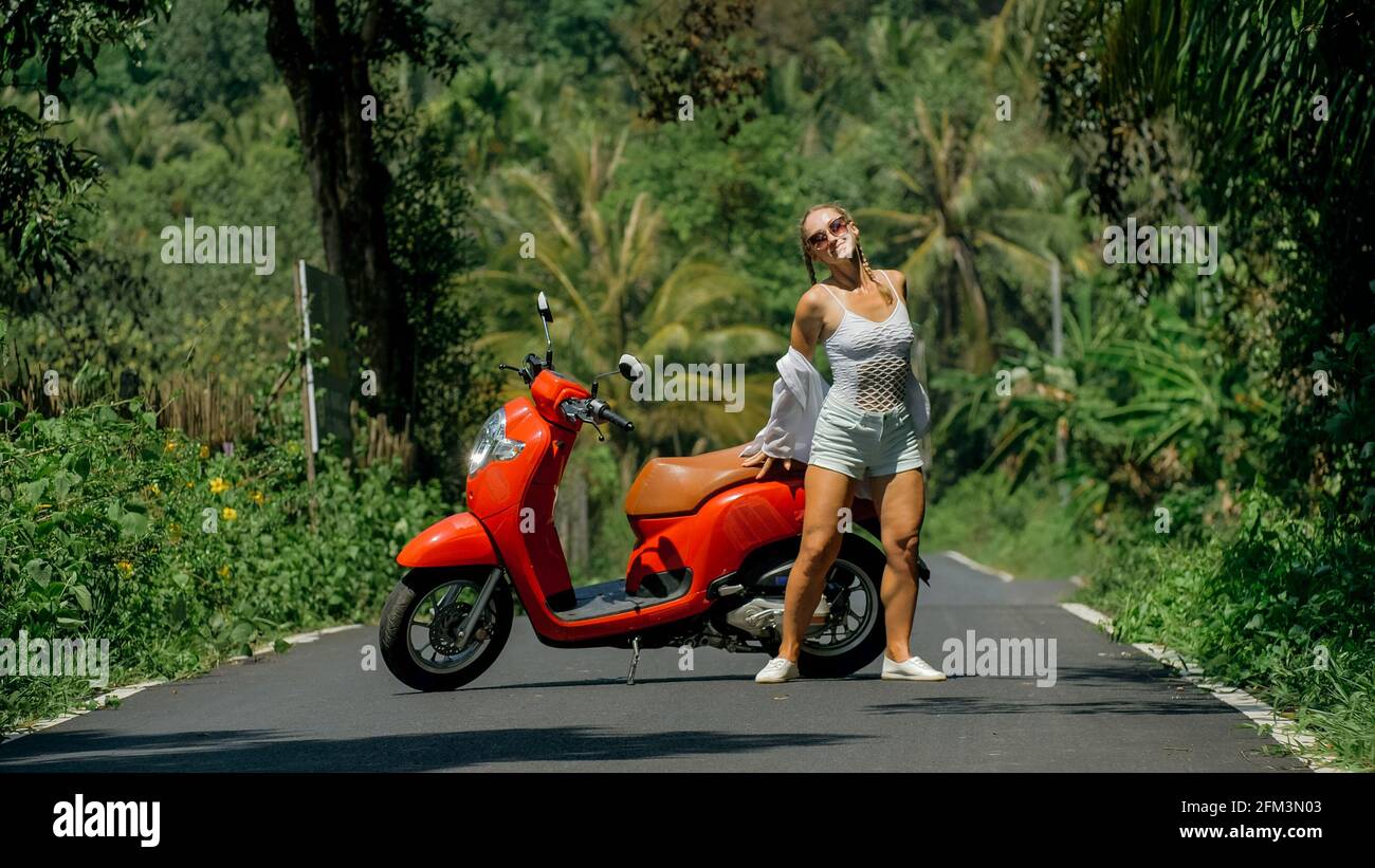 Woman on red scooter in white clothes drive on forest road trail ...