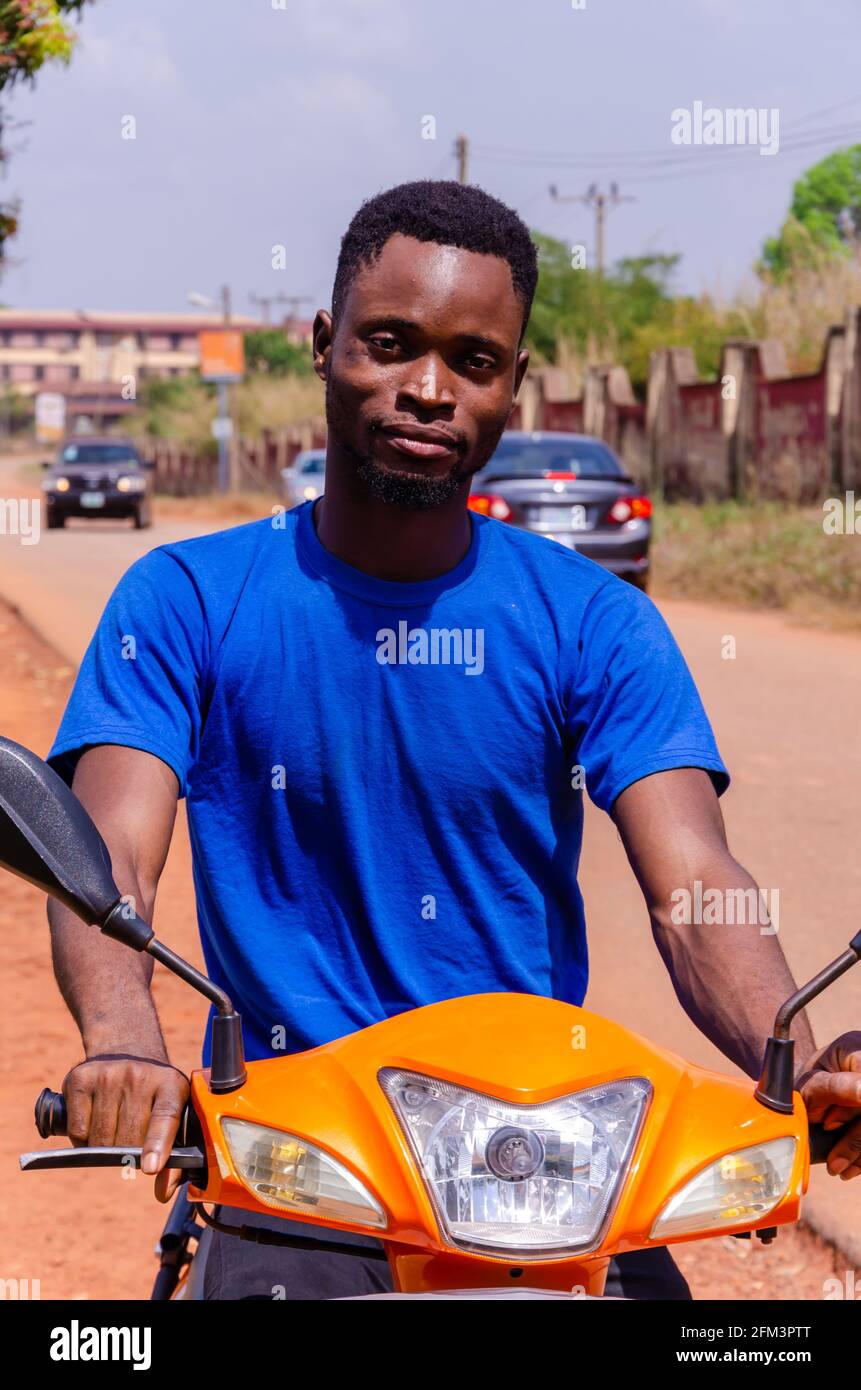 Nigerian biker on his motorcycle looking at the camera on a road ...