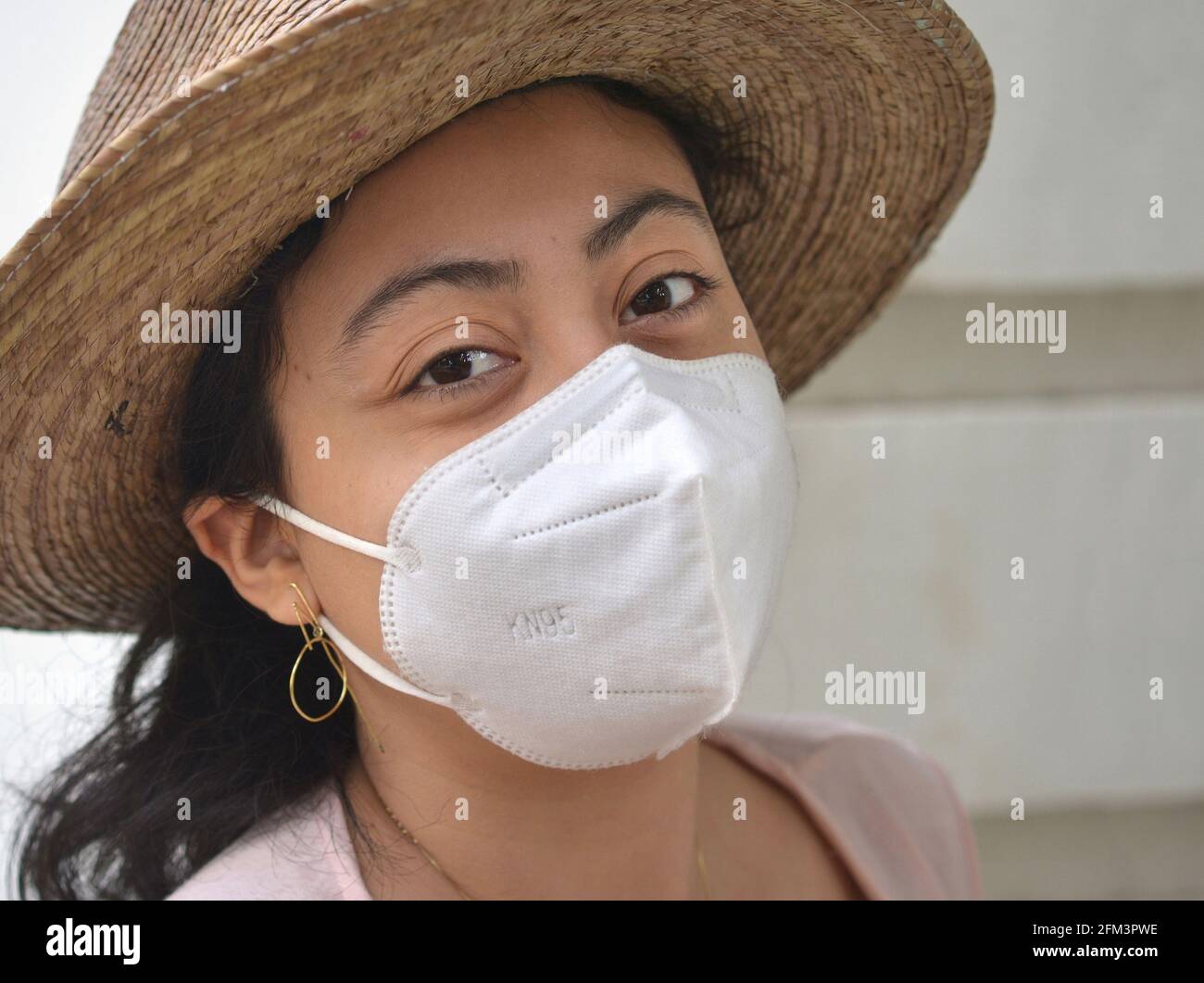 Brown-eyed young Mexican woman wears a worn Panama summer straw hat and ...
