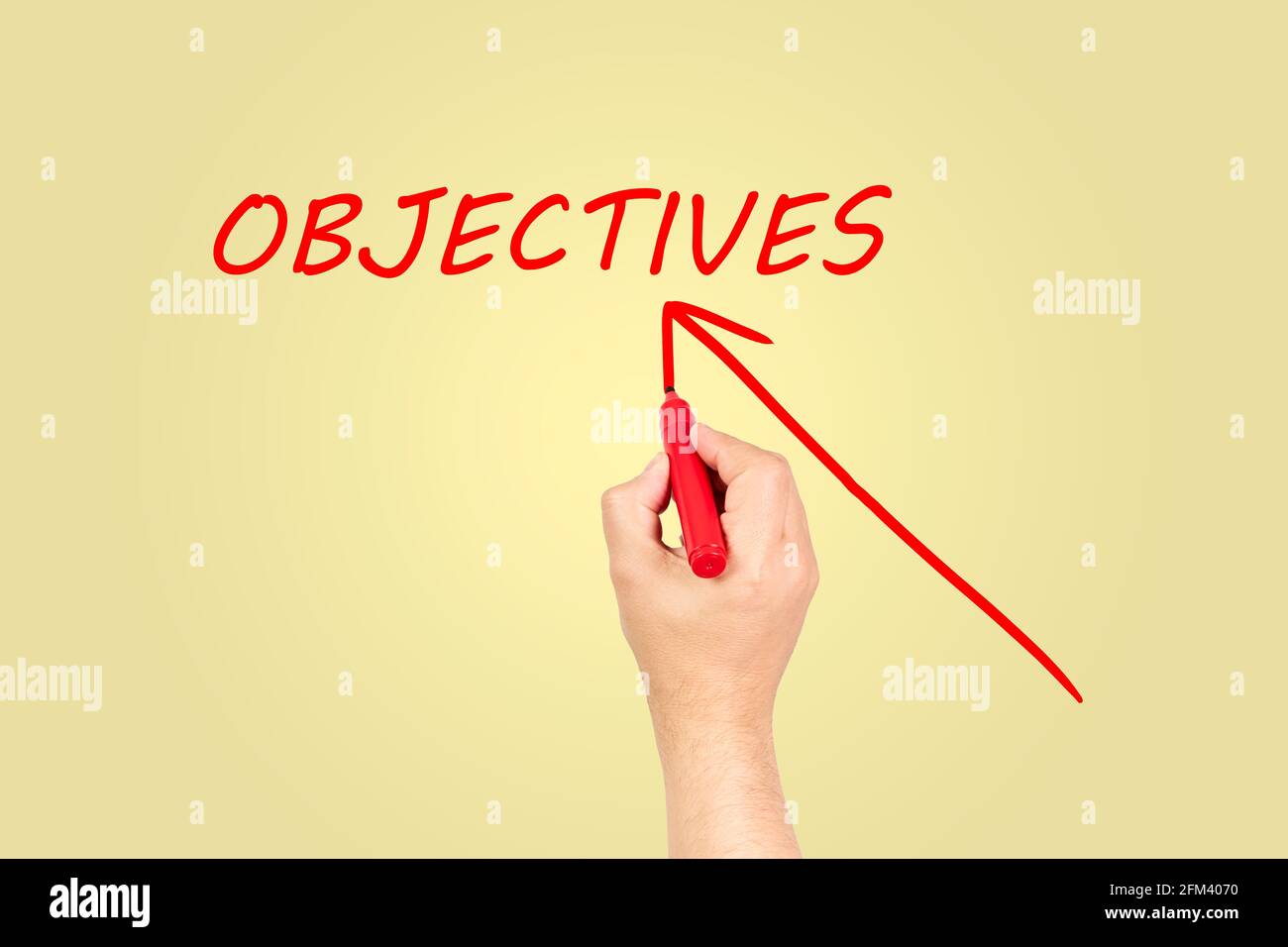 Hand of a man drawing an arrow next to the word Objectives on a yellow ...