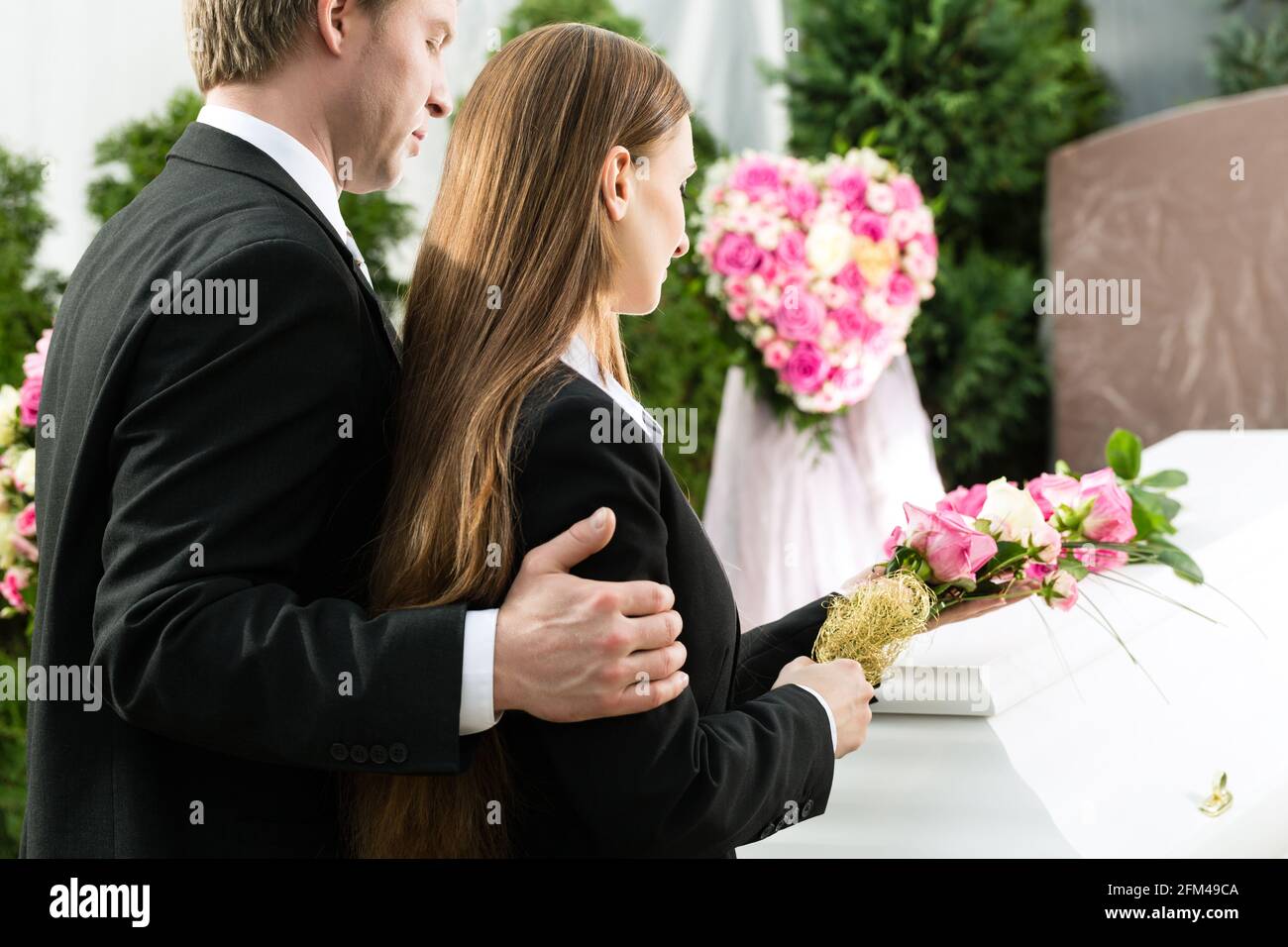 Mourning man and woman on funeral with pink rose standing at casket or ...