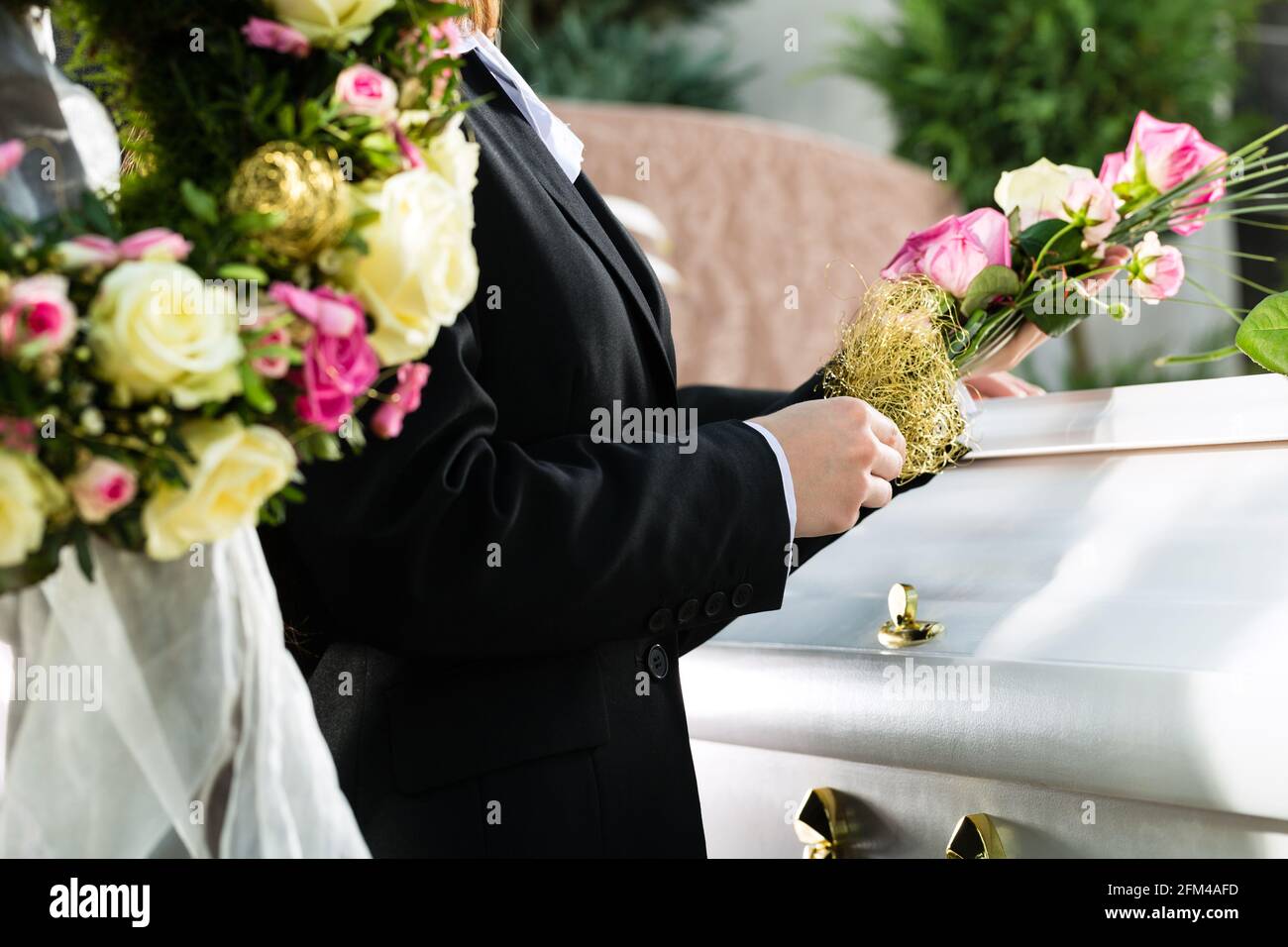 Mourning man and woman on funeral with pink rose standing at casket or ...