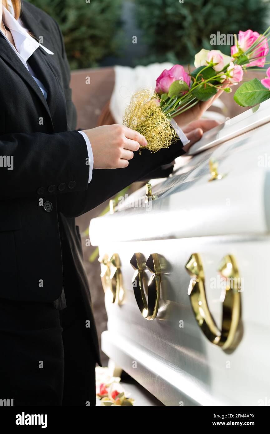 Mourning man and woman on funeral with pink rose standing at casket or ...