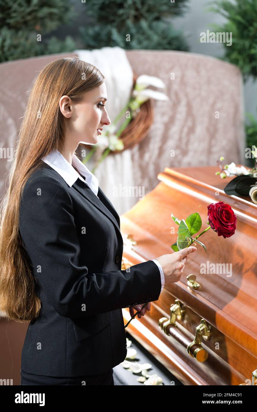 Mourning woman on funeral with red rose standing at casket or coffin ...