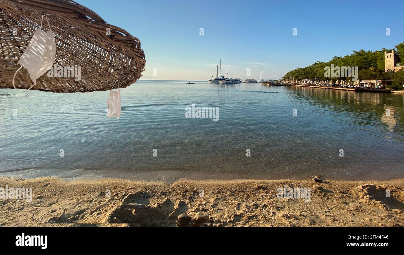 Face mask hanging on a straw beach umbrella in front of the sea ...