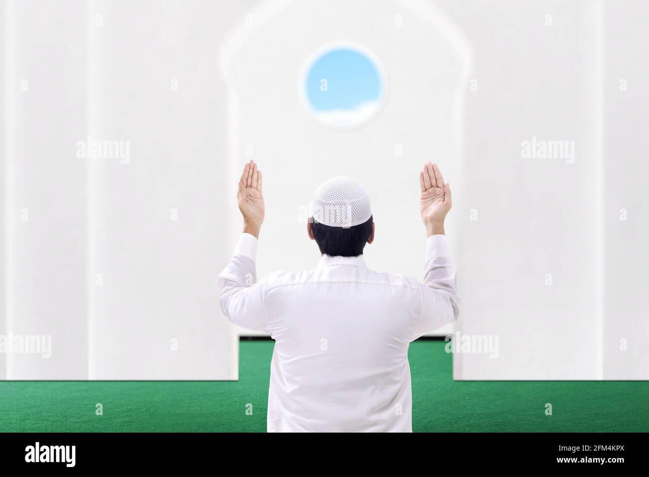 Rear view of Asian Muslim man sitting while raised hands and praying on ...