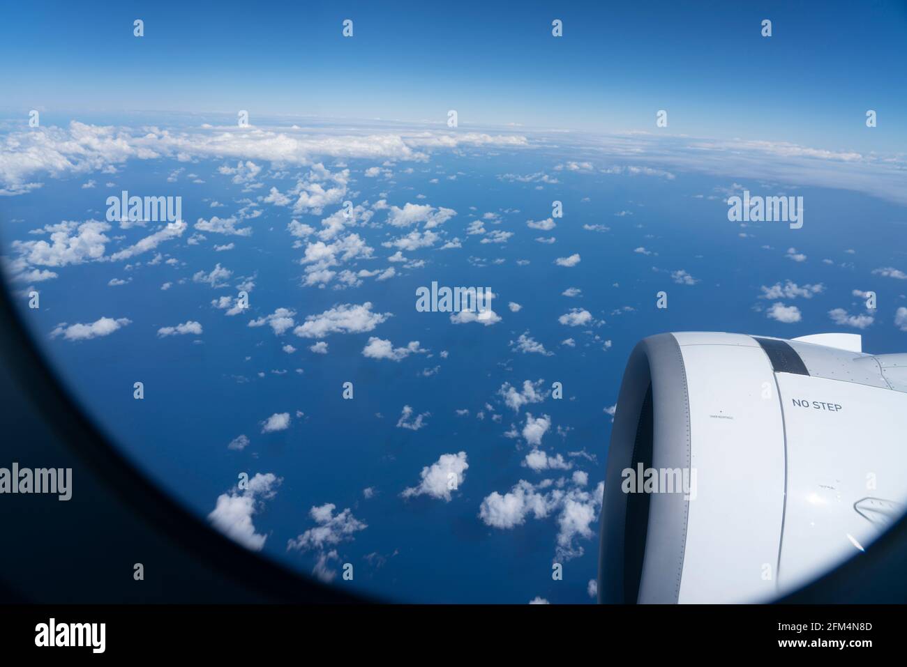 Plane engine and blue sky with small white clouds through window while ...