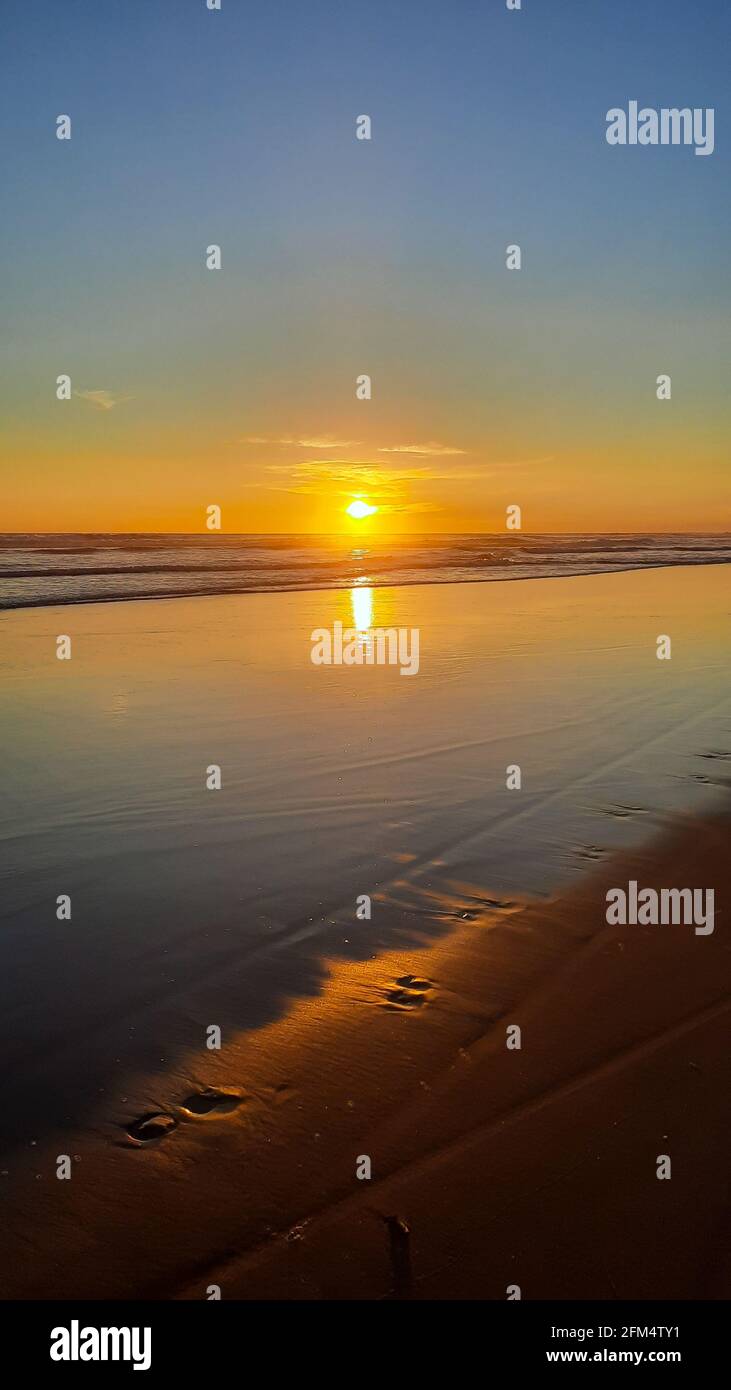 Wide wet sand beach reflecting orange sunlight while sunset Stock Photo ...