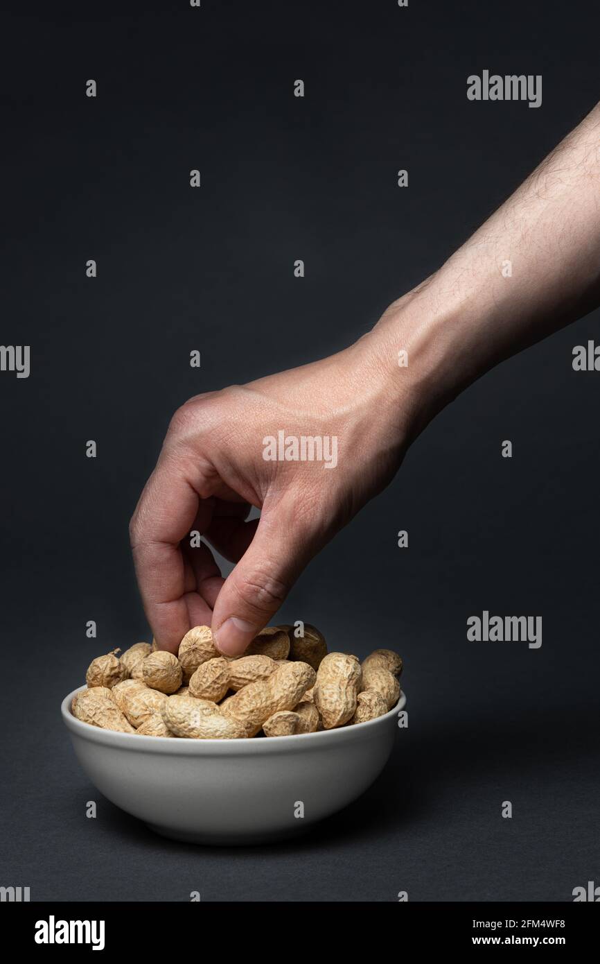 Man hand picking unpeeled peanuts from a bowl Stock Photo - Alamy