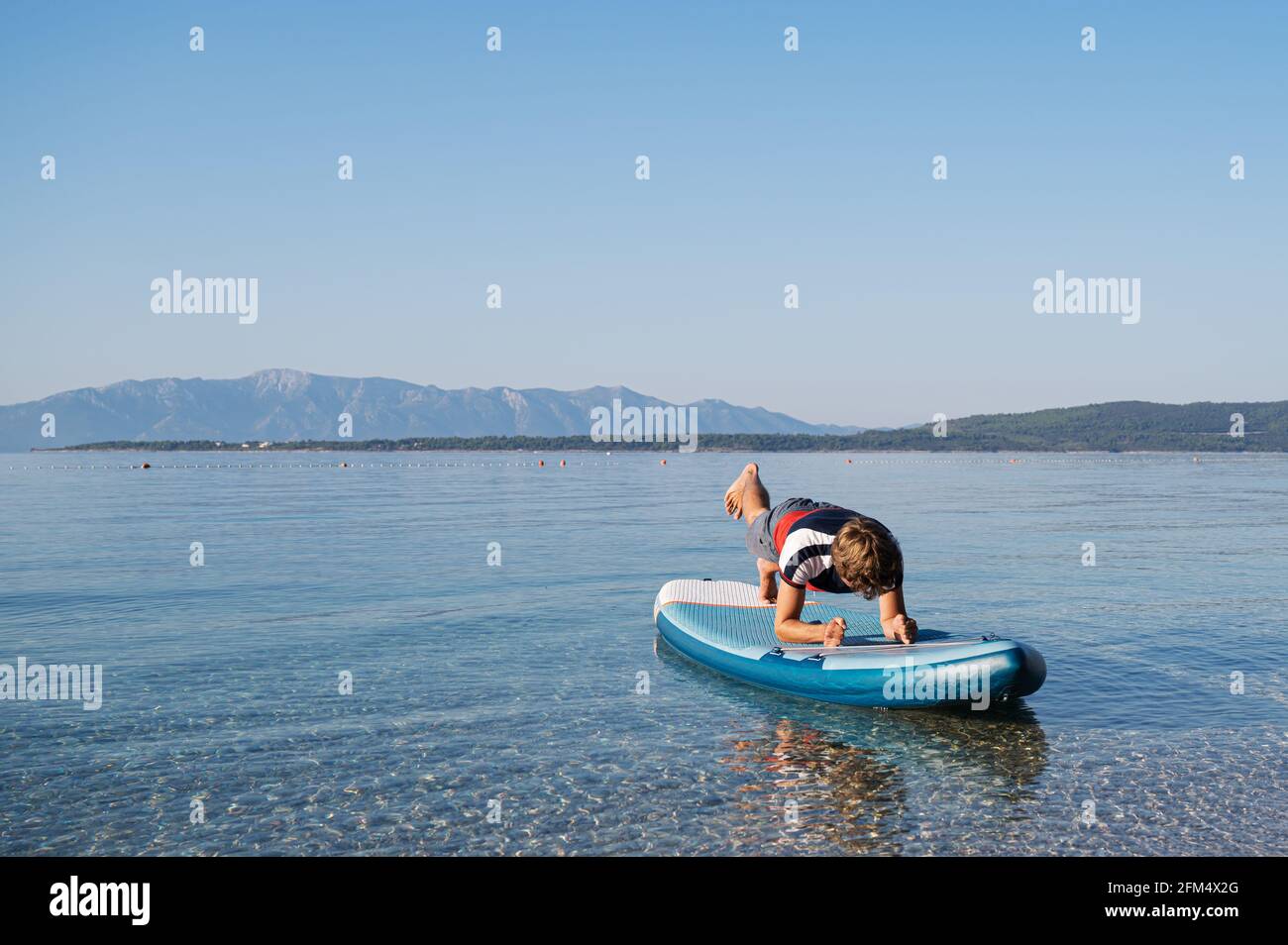 Fit young man making a plank exercise balancing on sup board floating ...
