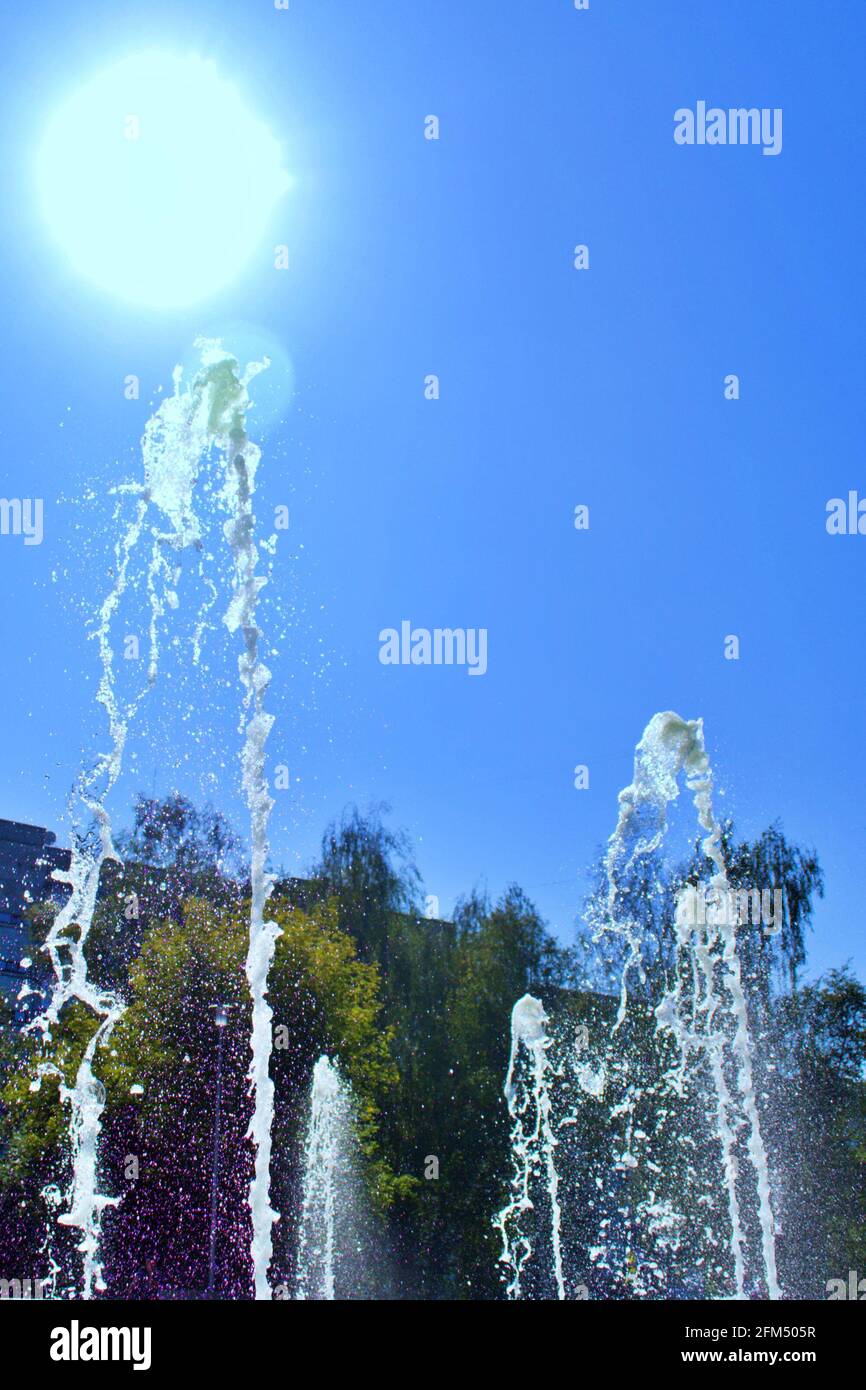 strong fountain water jets against backdrop of bright sun in summer ...