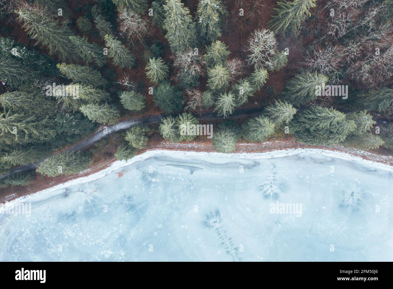 aerial view from a drone of a forest in the snow, and a frozen icy lake ...