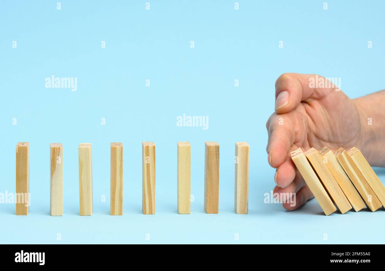 hand stops the fall of wooden bars on a blue background. The concept of ...