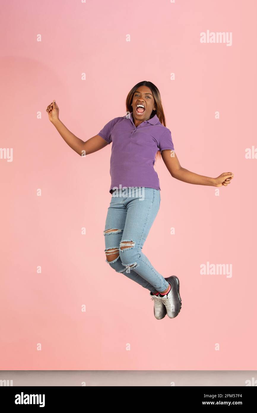 One happy African young girl jumping isolated on pink studio background ...