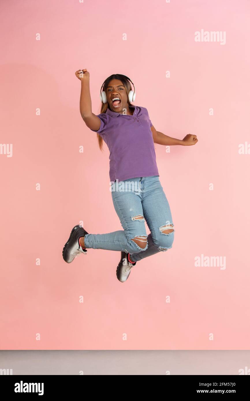 One happy African young girl jumping isolated on pink studio background ...