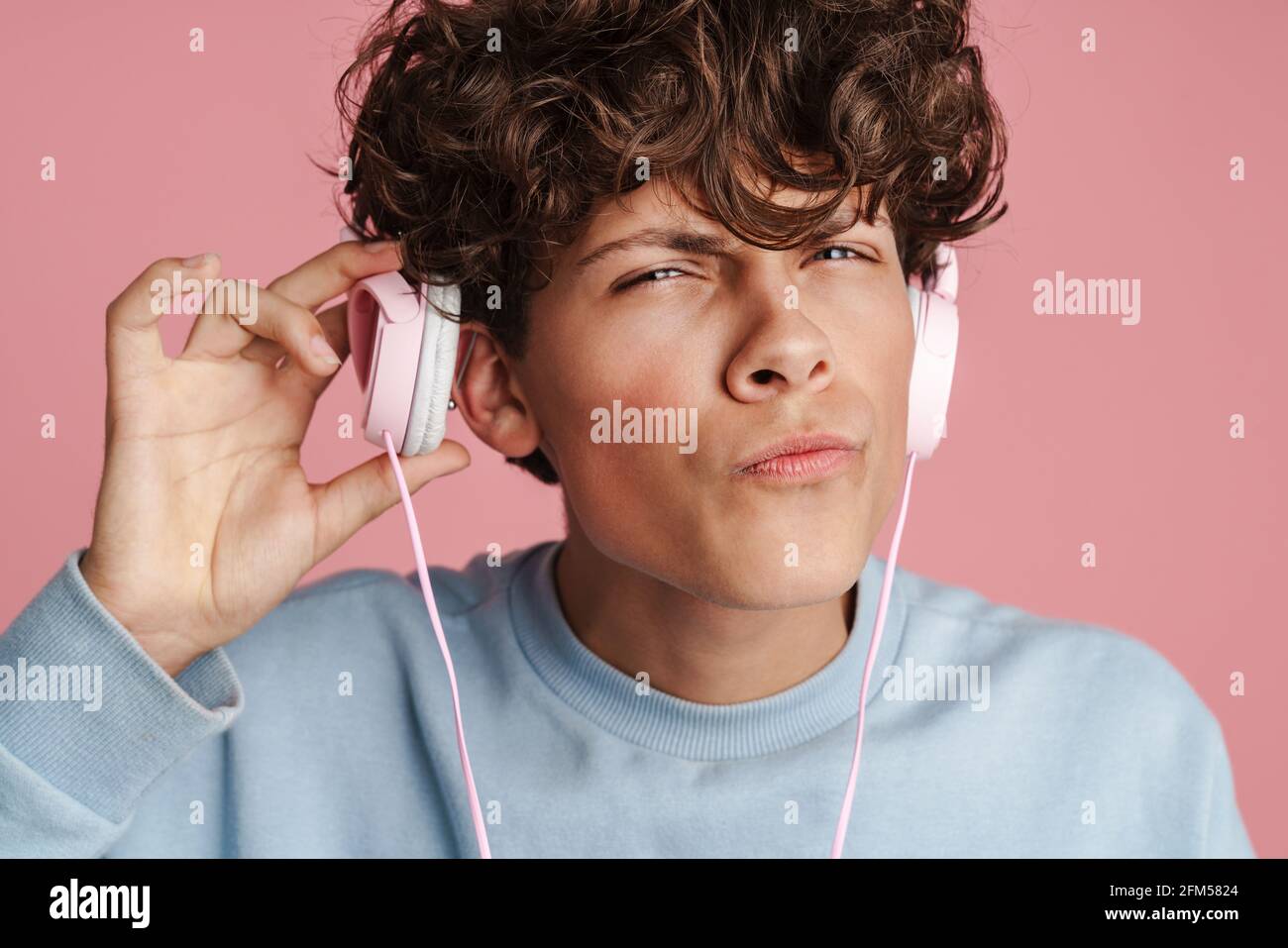Confused young guy removing headphones from ear and looking at camera ...