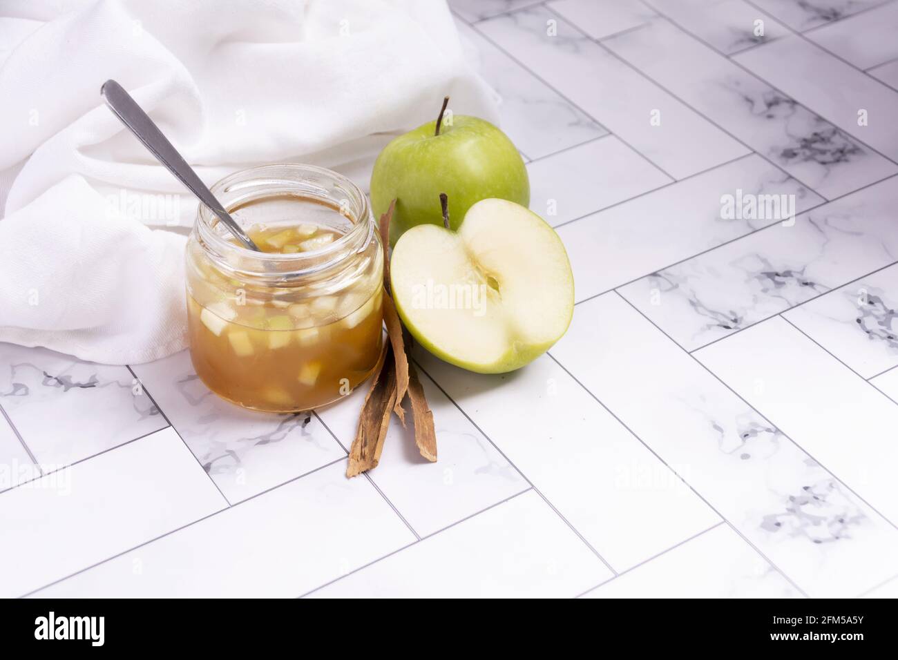 Green apples, cinnamon and a jar of apple jam on a white background ...