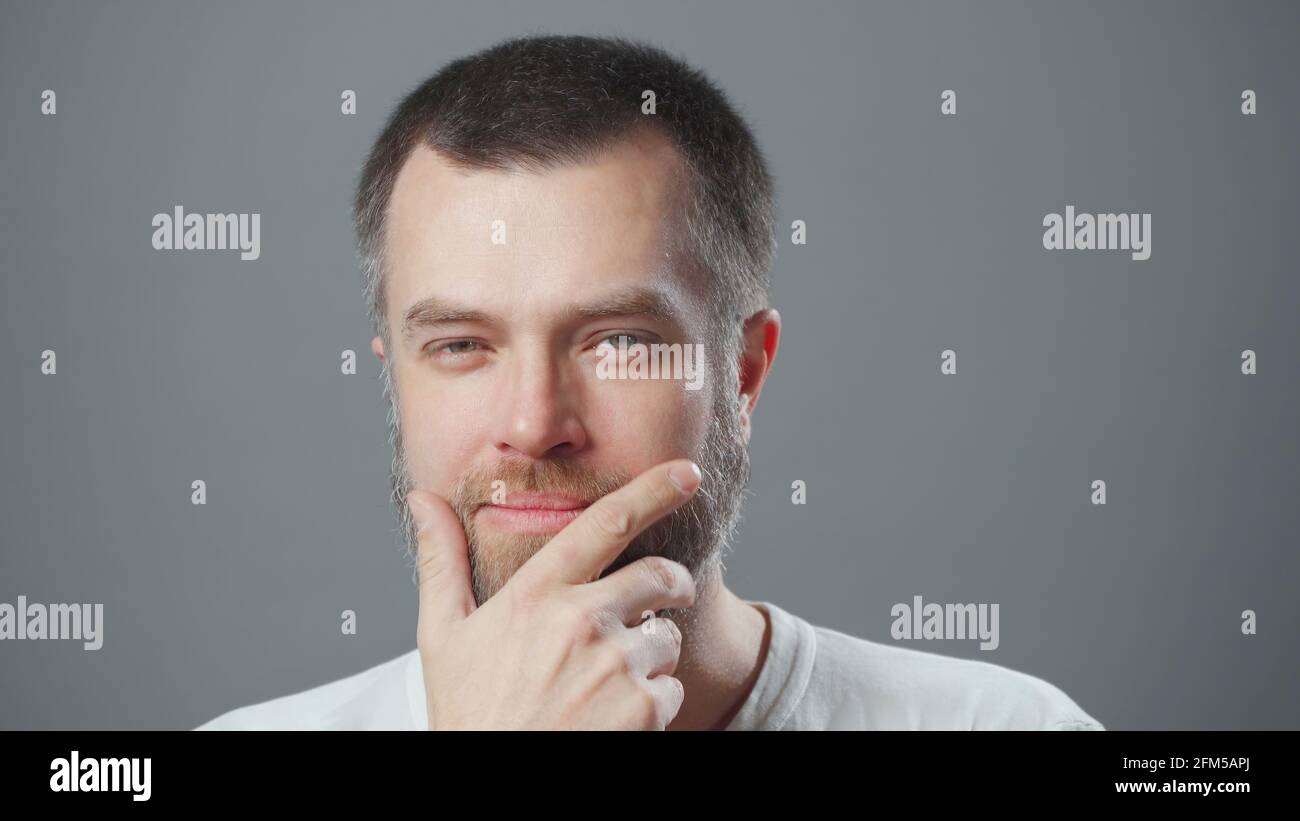 Photo of man stroking beard on grey Stock Photo - Alamy