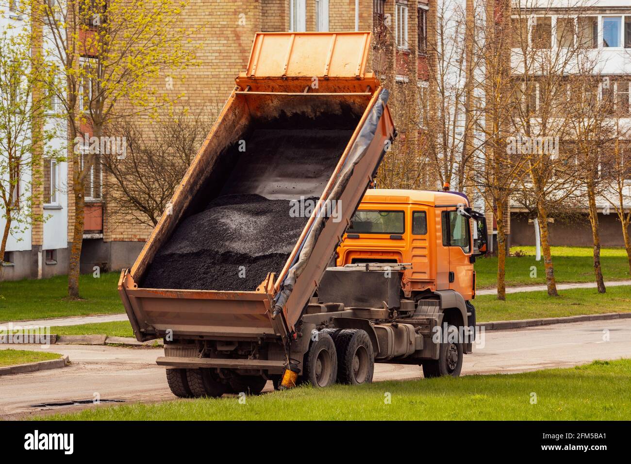 Tipper unloading fresh asphalt from body during road construction works ...