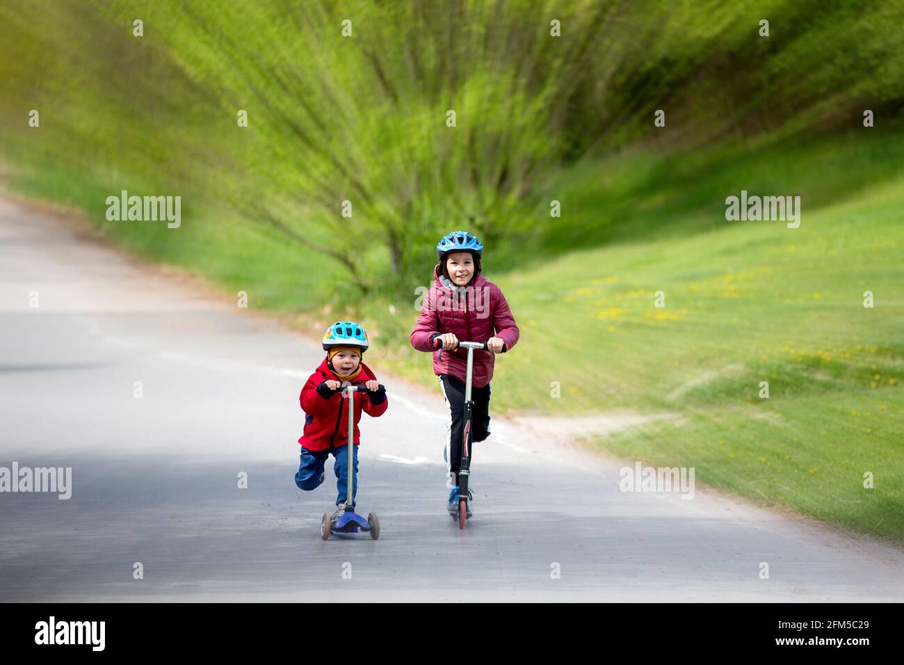 Children, brothers, riding scooters in the park together, spring sunny ...
