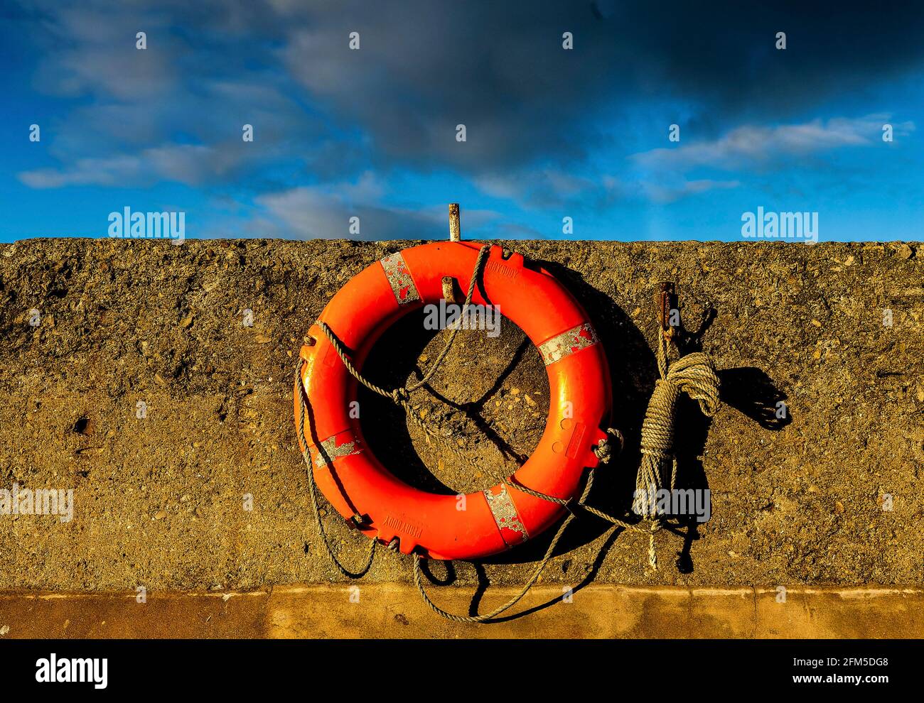 Red life preserver tied to the harbor wall Stock Photo - Alamy