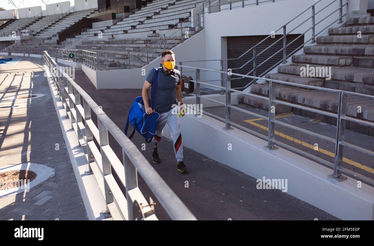 Caucasian male athlete with prosthetic leg wearing face mask walking in ...