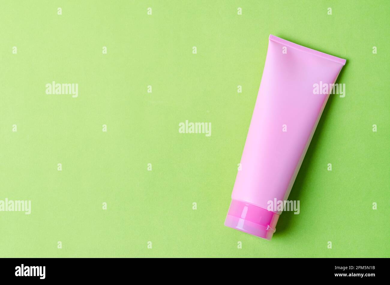 Empty a cosmetic pink tube of cream on green background with empty ...