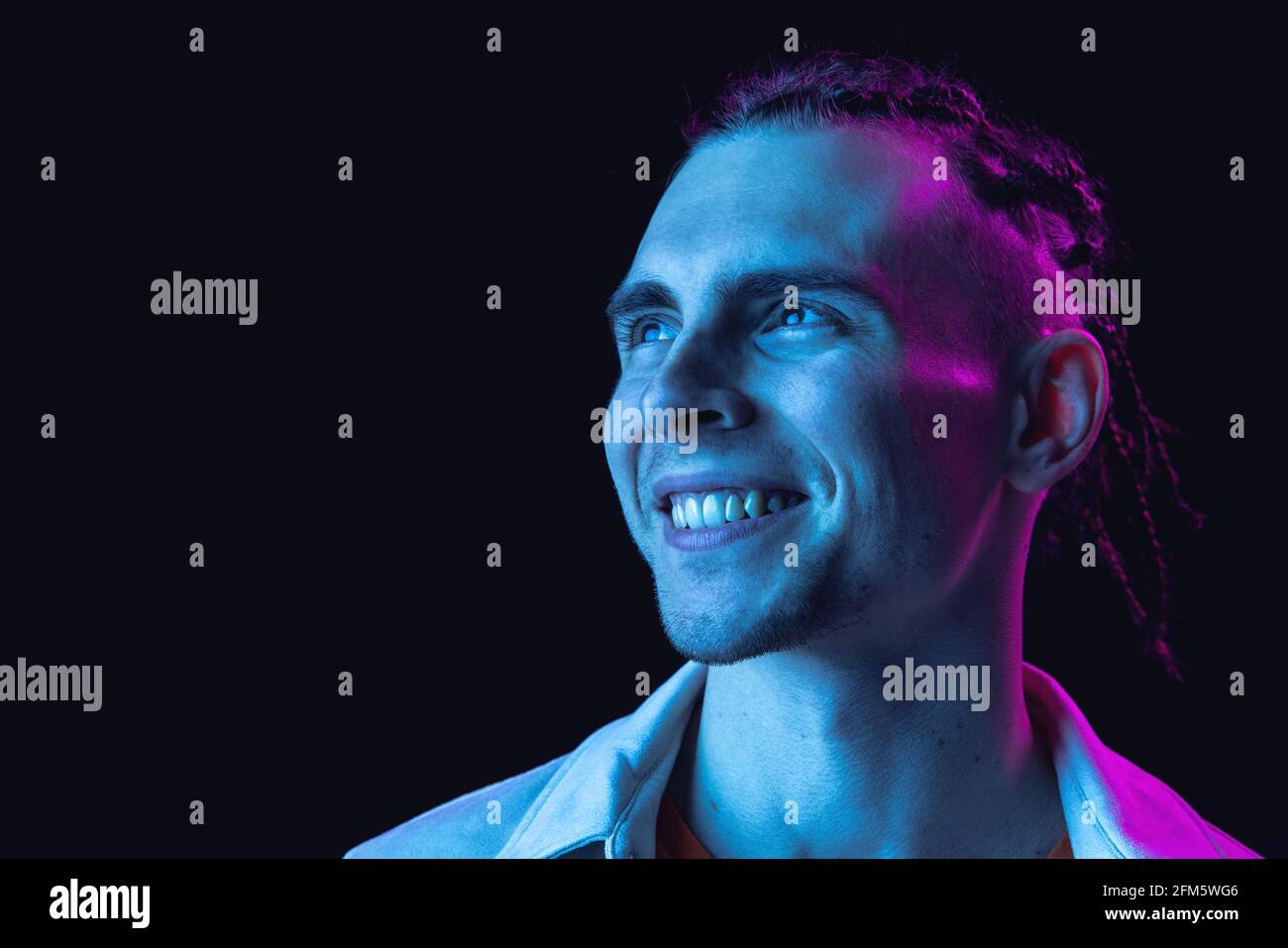 Caucasian young man's portrait on dark studio background in neon ...
