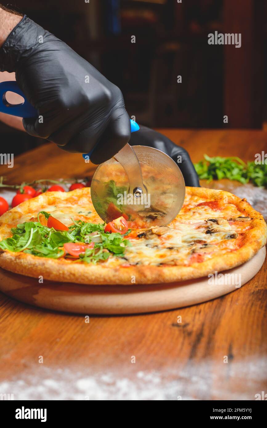 Vertical close up photo of a chef in black rubber gloves slicing pizza ...