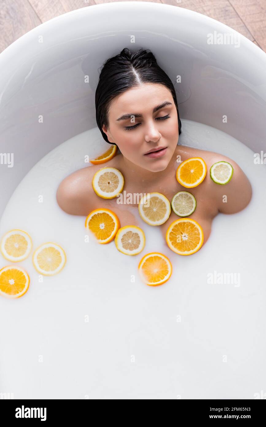 overhead view of young woman in milky bath with fresh citrus slices ...