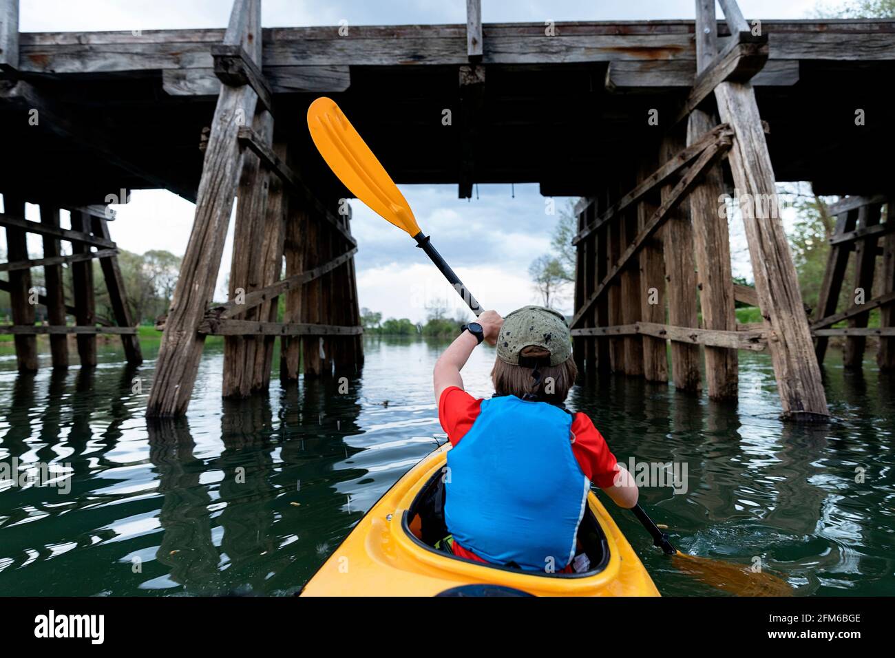 Rear view of a young boy kayaking under wooden bridge over the river ...