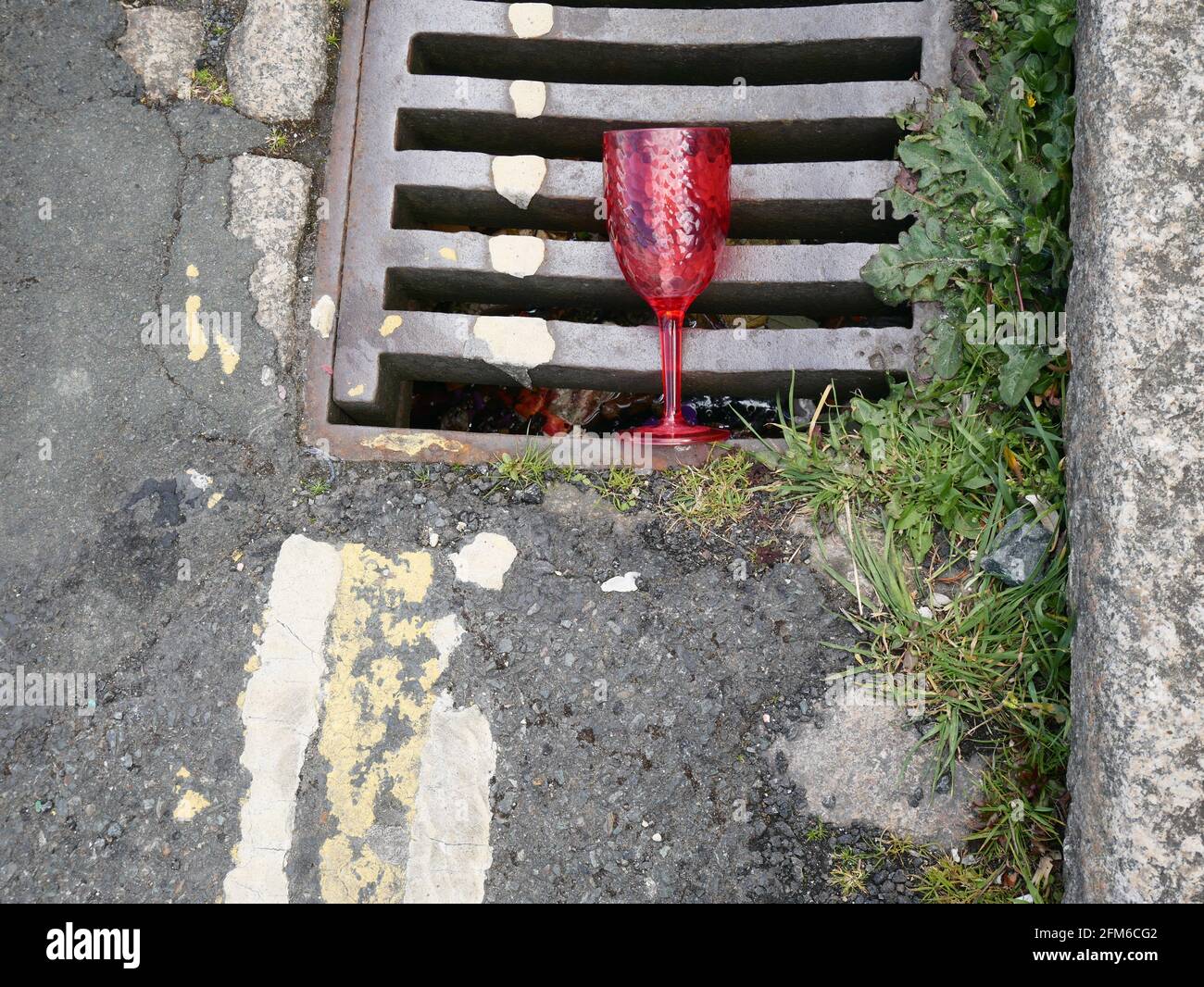 Red party drink glass abandoned over drain in roadside gutter Stock ...