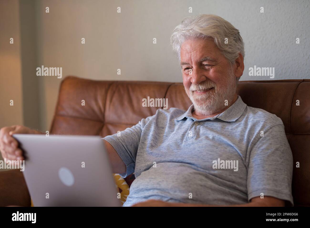 Happy aged man indoor working at laptop and smiling, relaxed senior ...