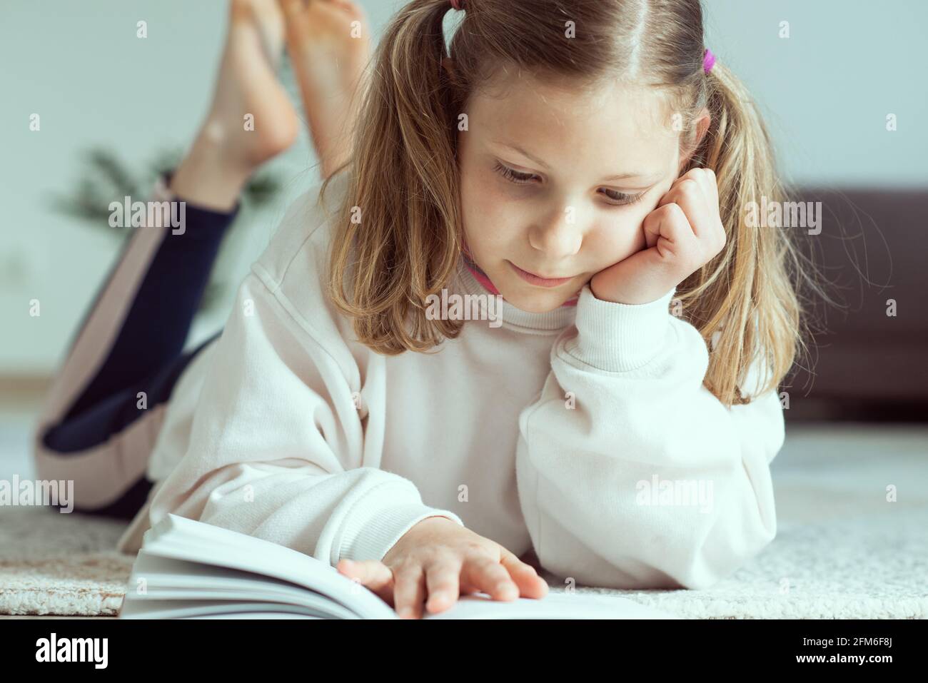 Portrait of cute teen girl reading book on floor of living room at home ...