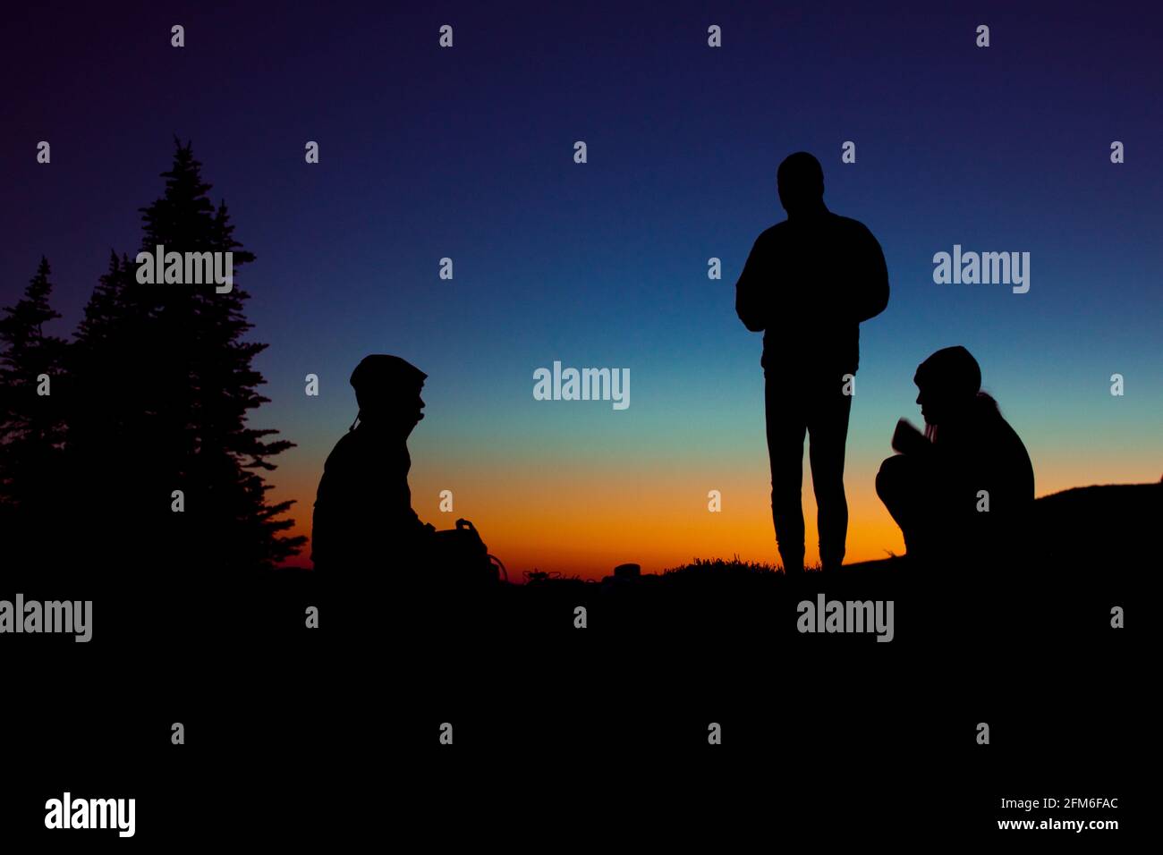 Group of three people enjoy an evening while camping in the mountains ...
