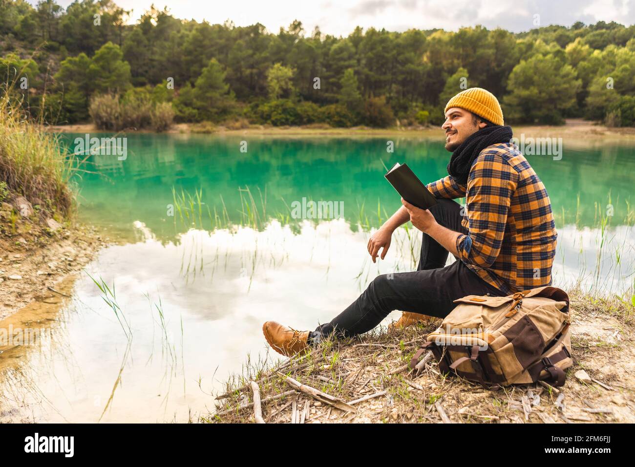 Spanish traveler enjoying reading a book sitting on a peaceful lake ...
