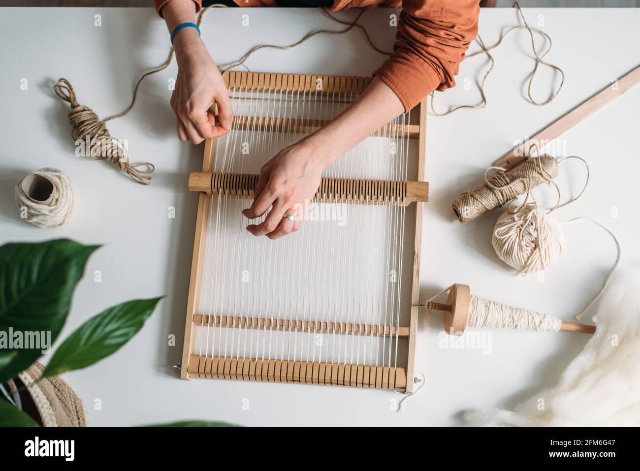 Hands of woman weaving wool rug at the table with flowers and threads ...