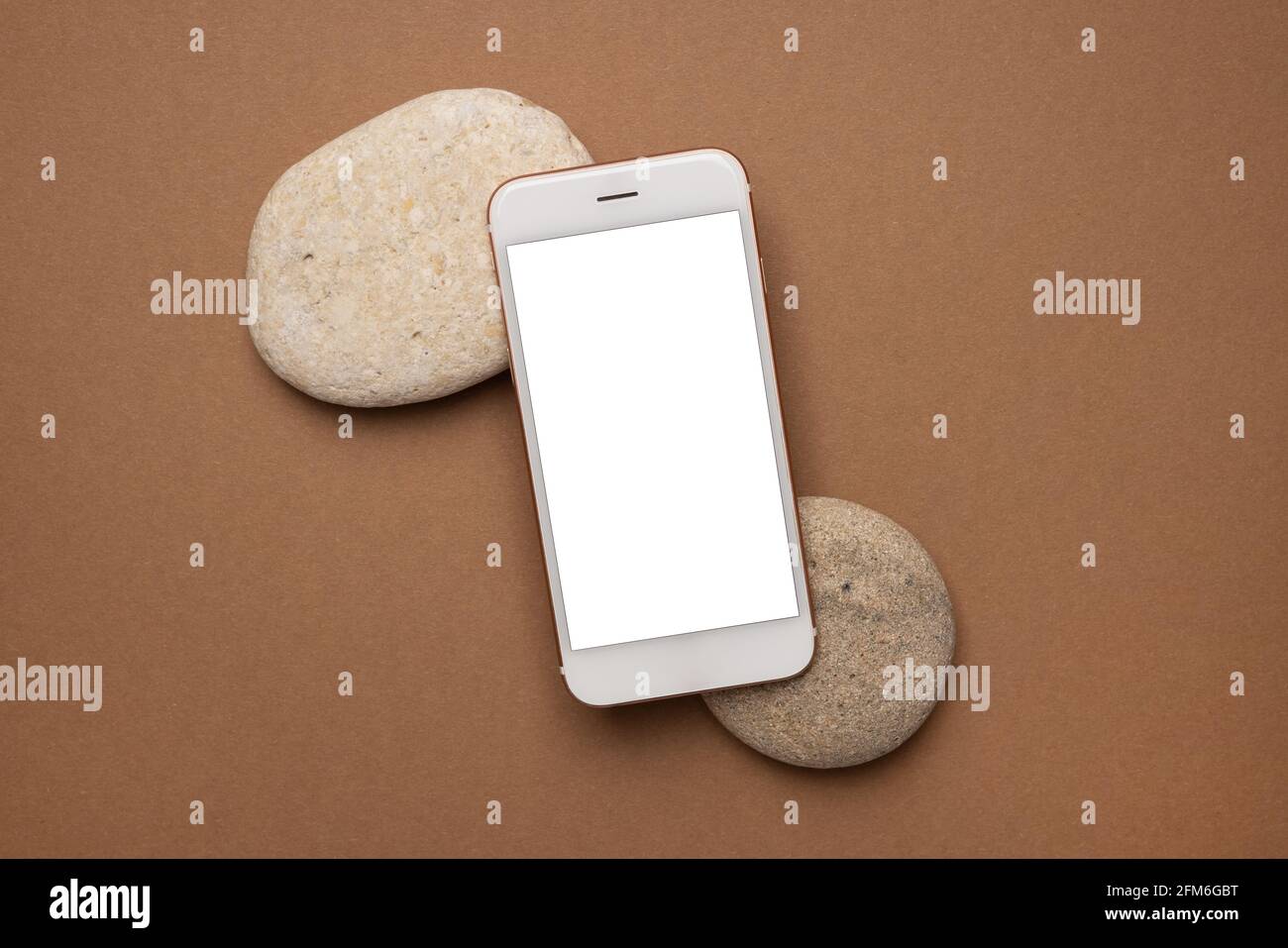 Mobile phone with white screen and stone on a light brown background ...