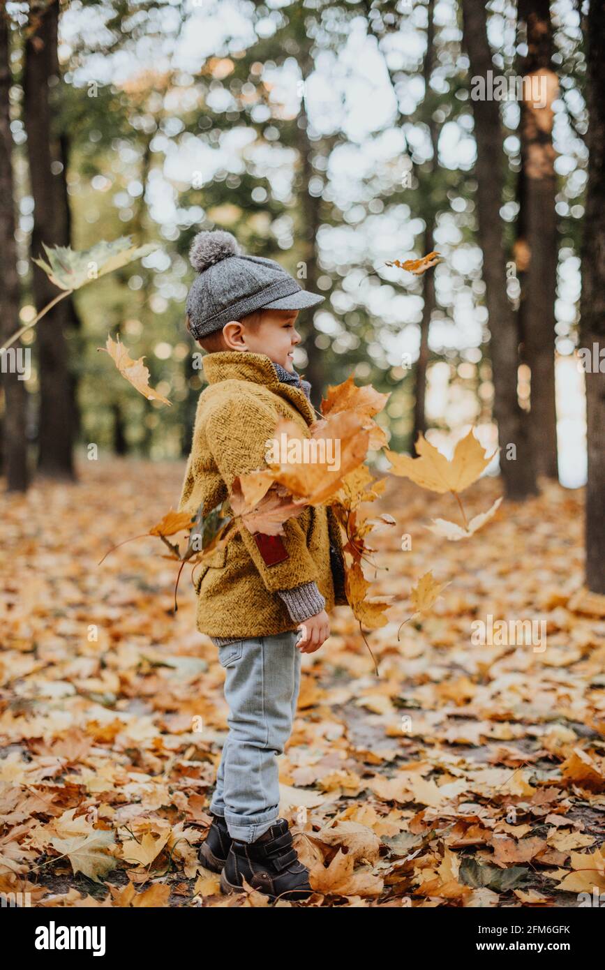 Stylish boy having fun in autumn city park. Happy kid playing woth ...